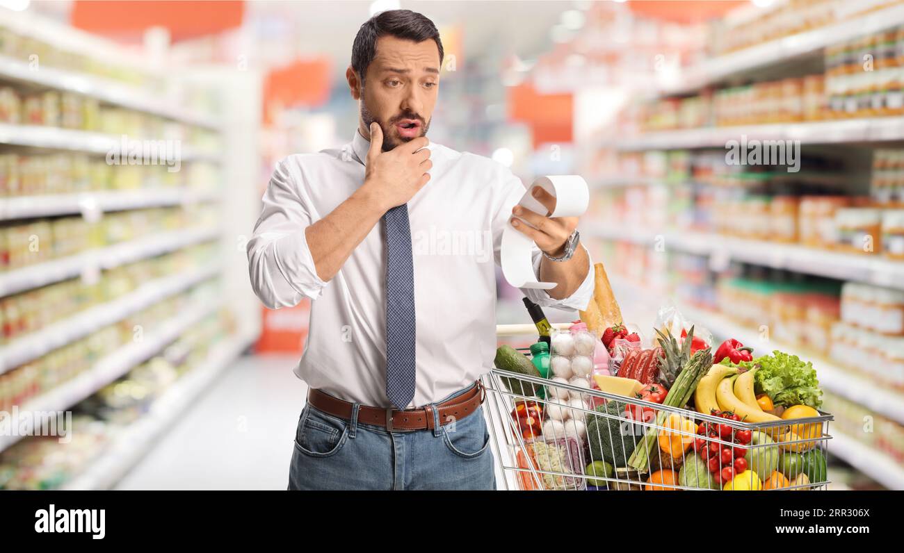 Confused man with a shopping cart holding a bill at a supermarket Stock ...