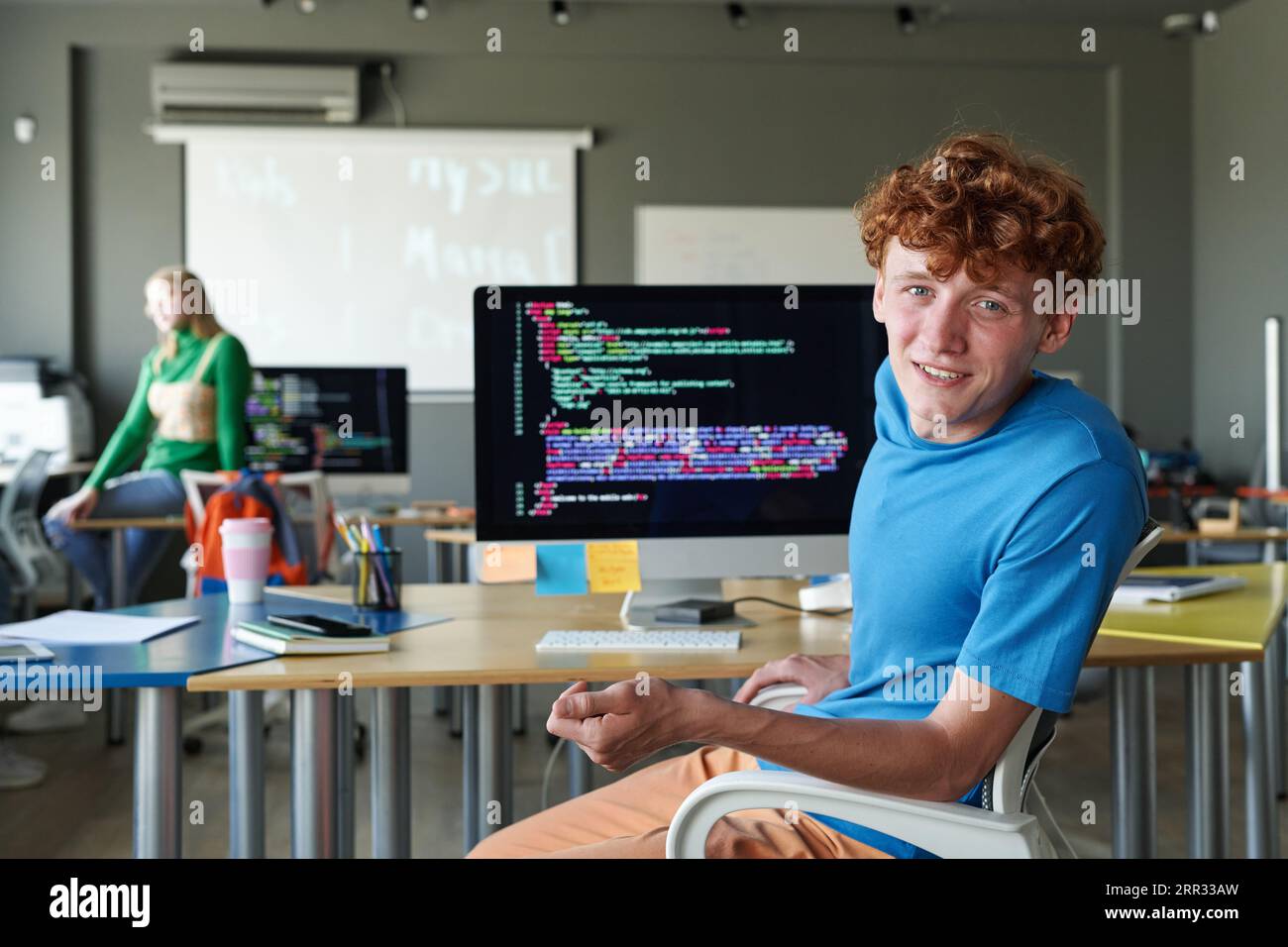 Portrait of schoolboy smiling at camera while working with computer codes on computer in the ...