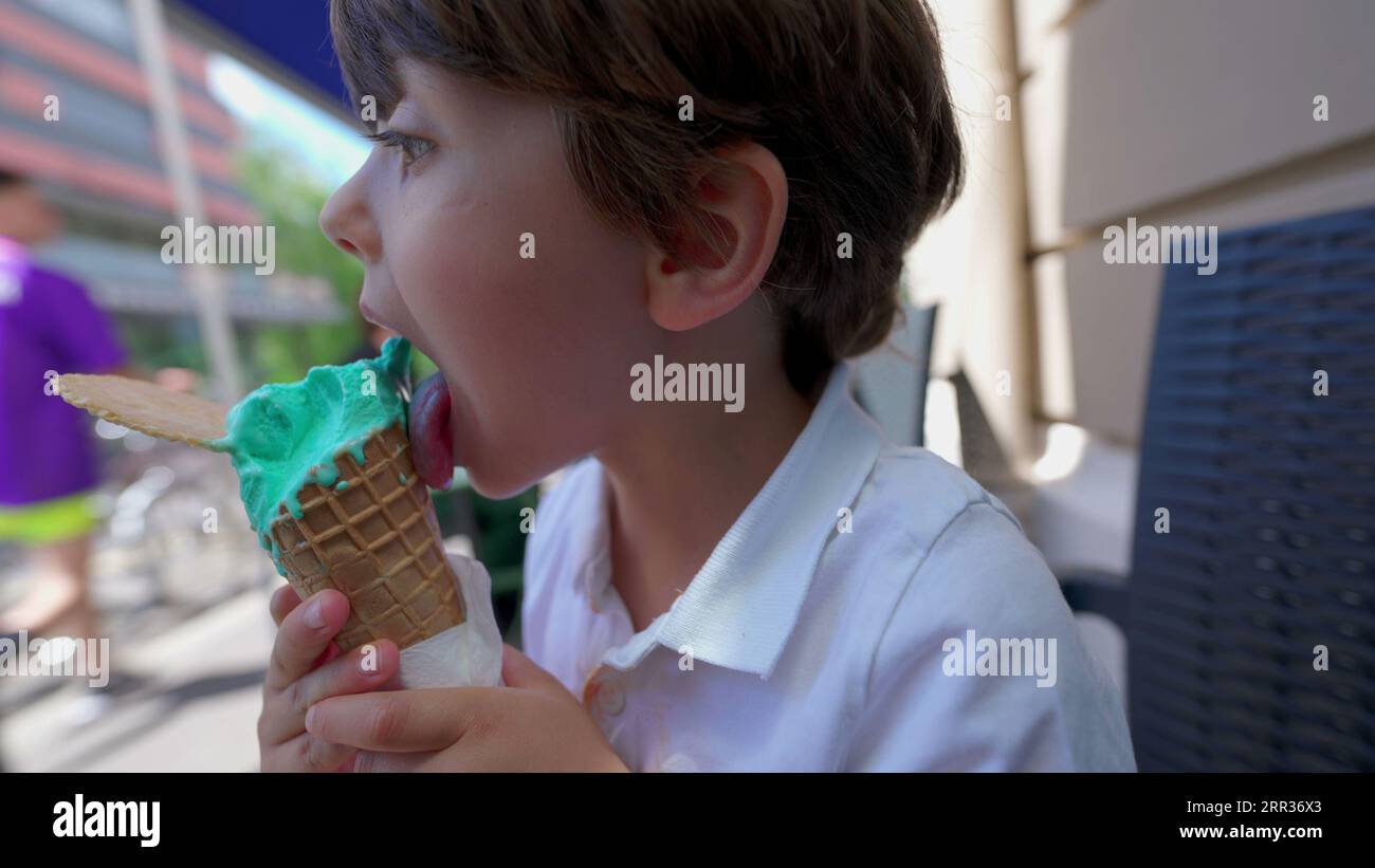 Small boy eating colorful icecream cone outside at parlor shop's ...