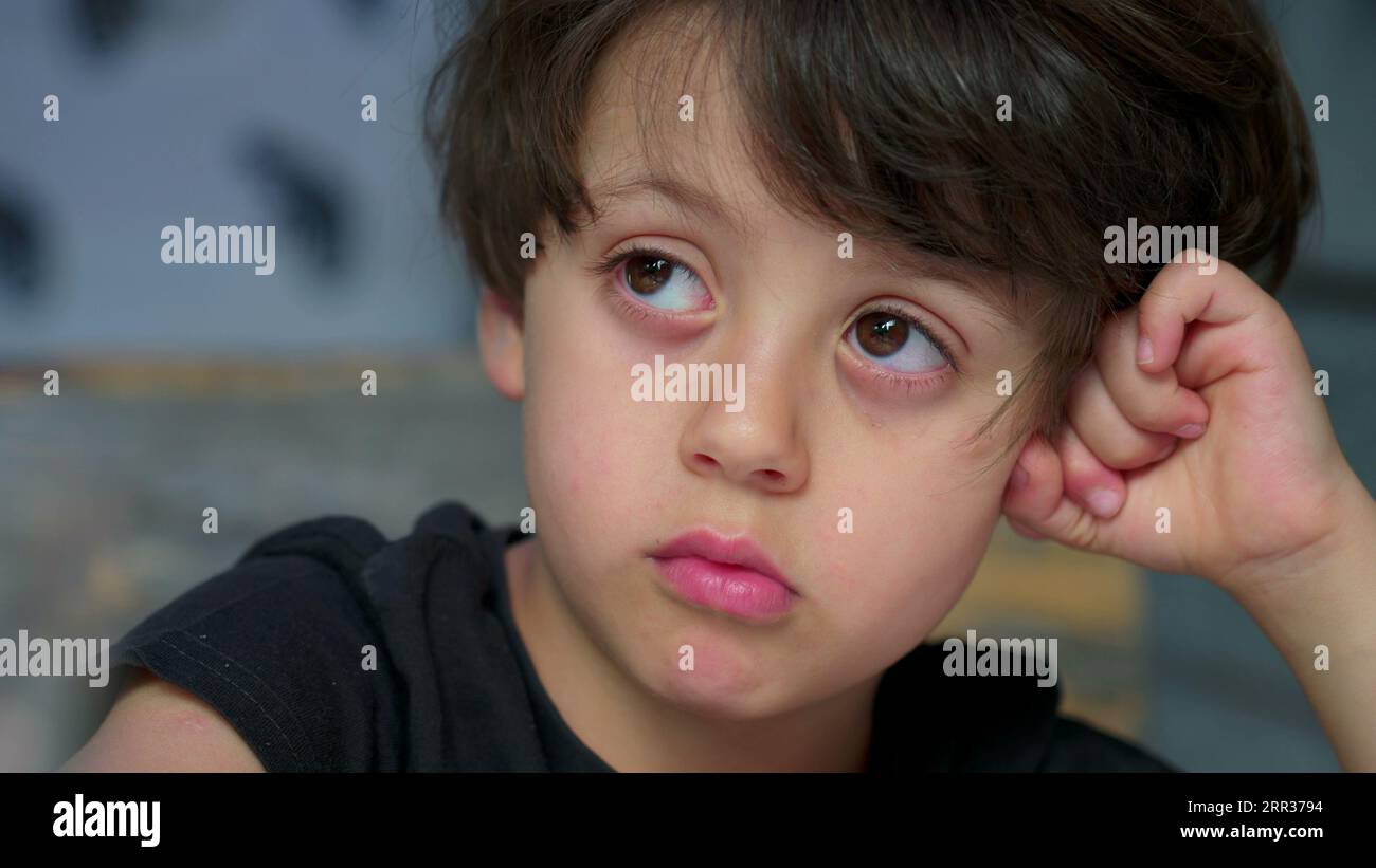 Close-up child face with bored expression. Pensive small boy struggles ...