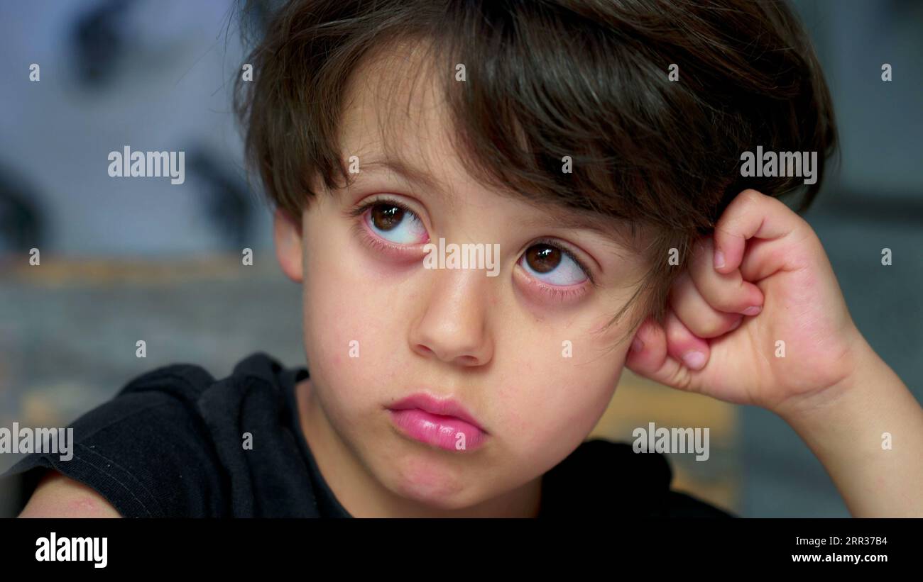 Close-up child face with bored expression. Pensive small boy struggles ...