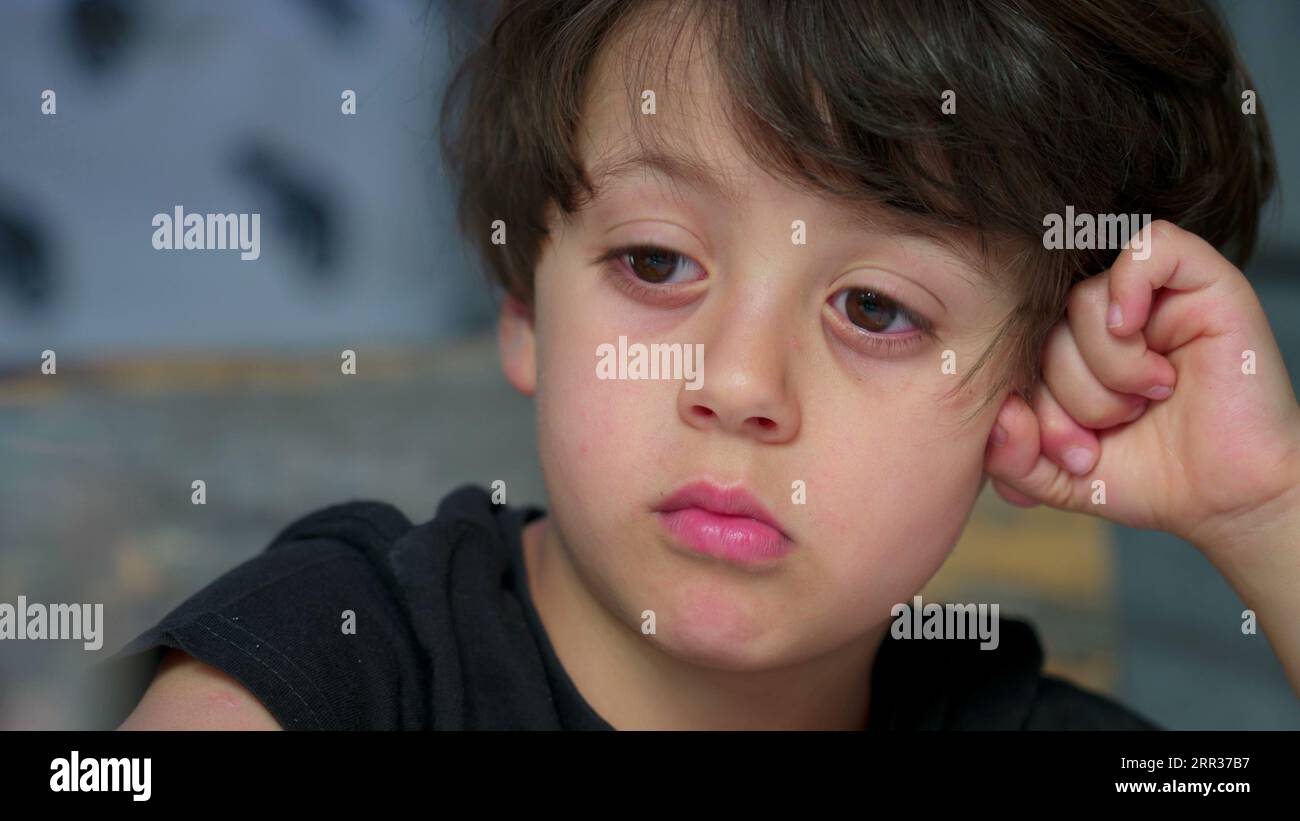 Close-up child face with bored expression. Pensive small boy struggles ...
