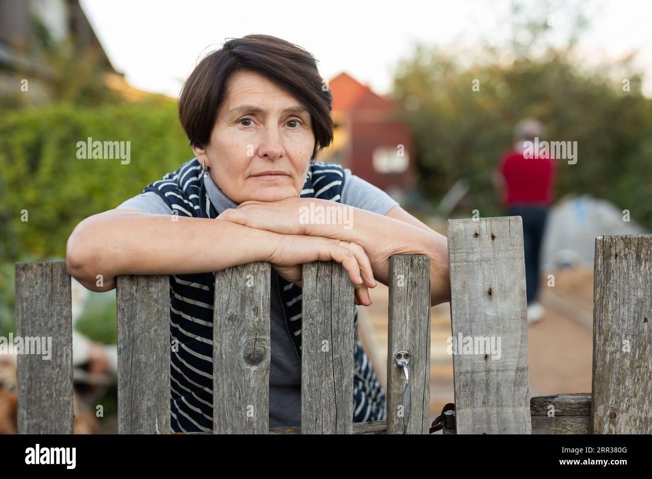 Portrait of an elderly woman at the fence of her farm on summer evening ...
