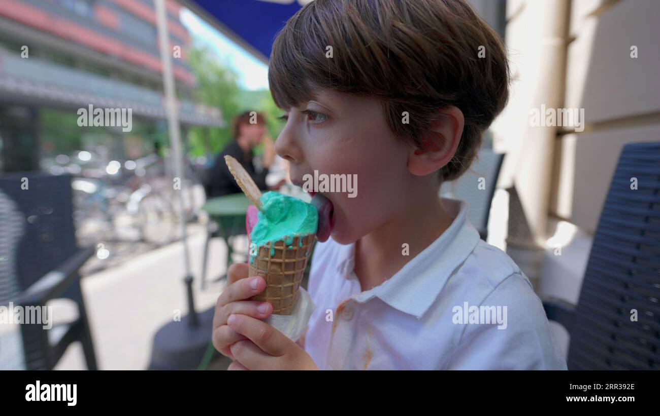 Small boy eating colorful icecream cone outside at parlor shop's ...
