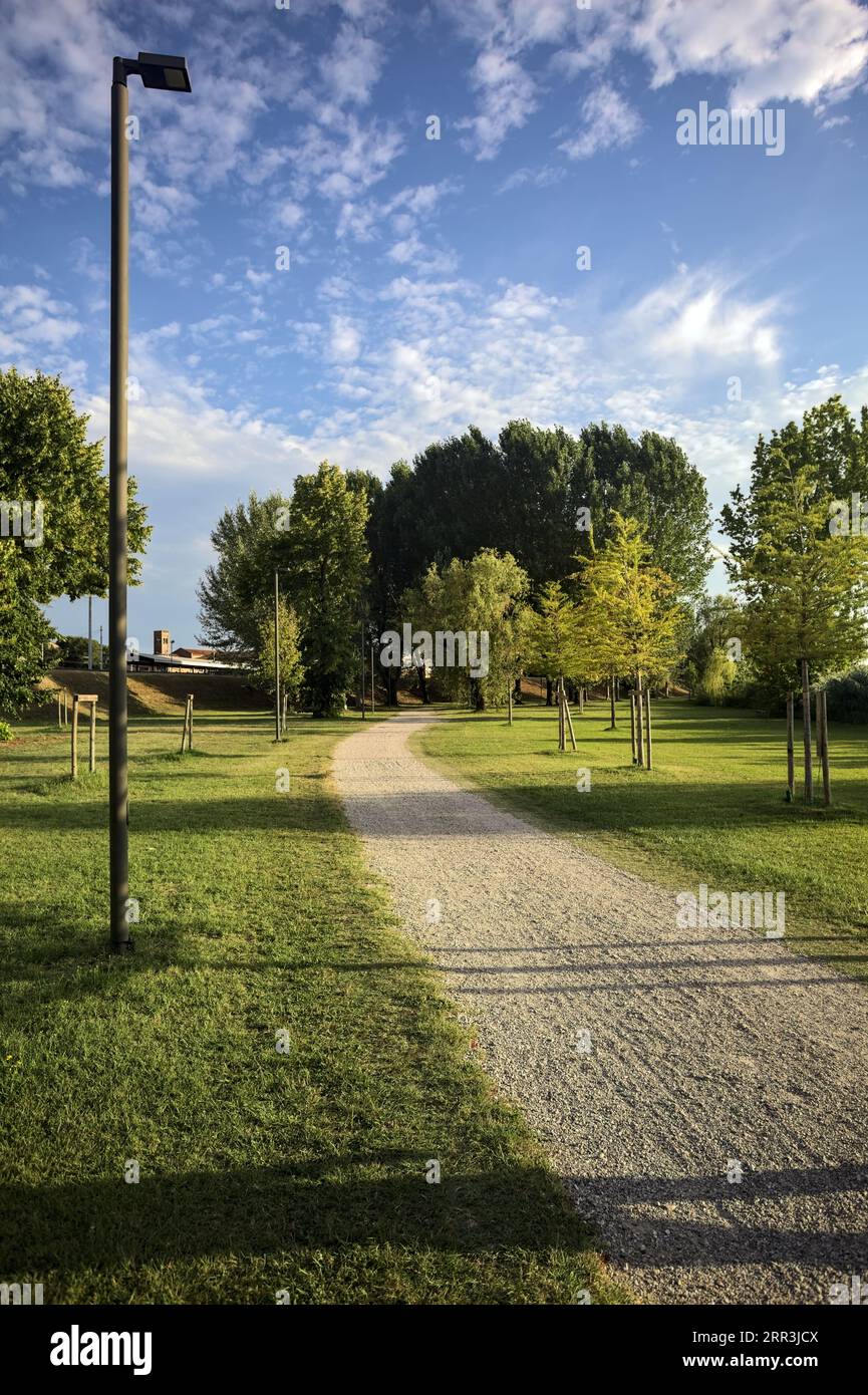 Path in a park with trees next to an embankment at sunset in an italian ...