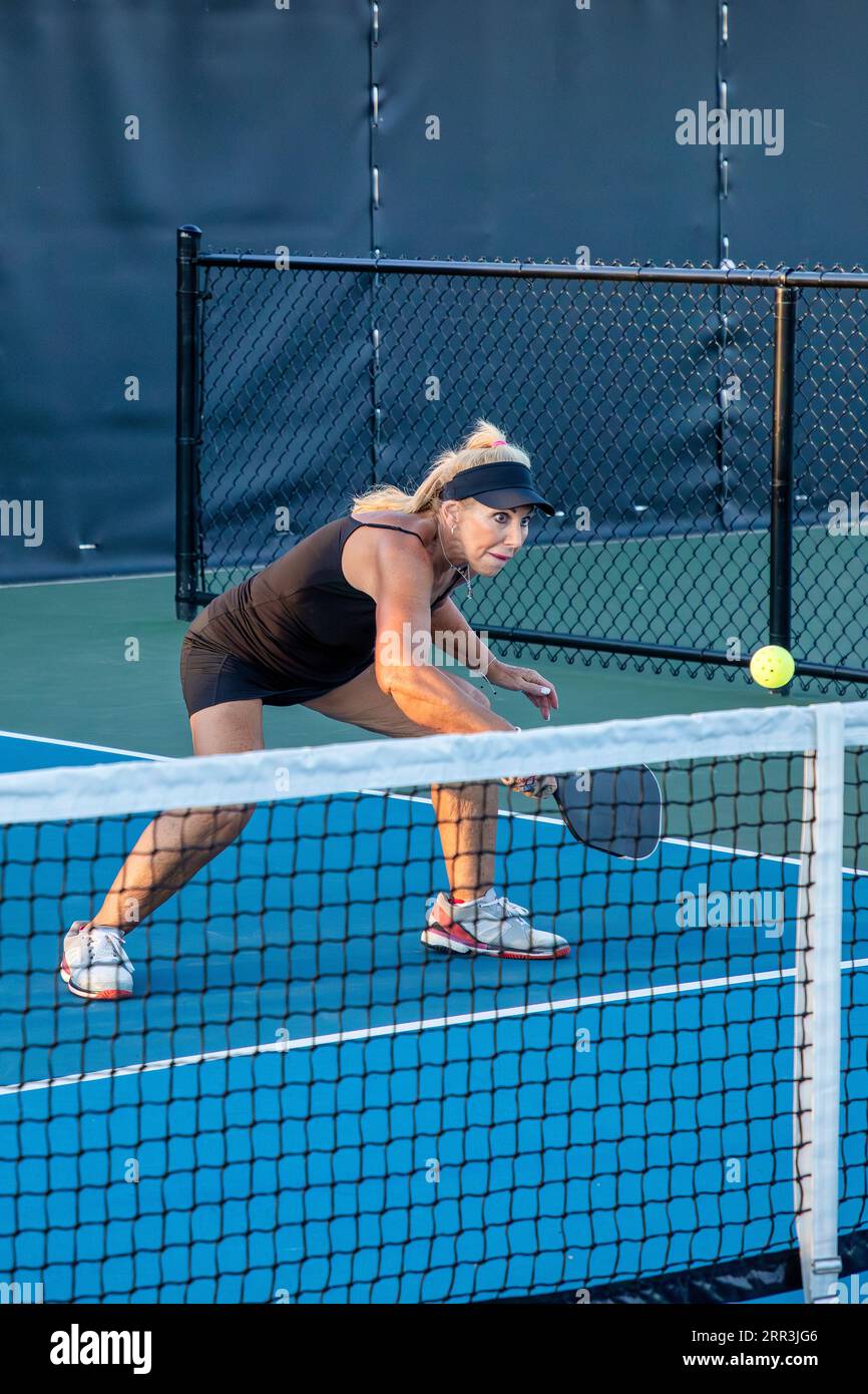 A female pickleball player returns a volley of a bright yellow ball at ...