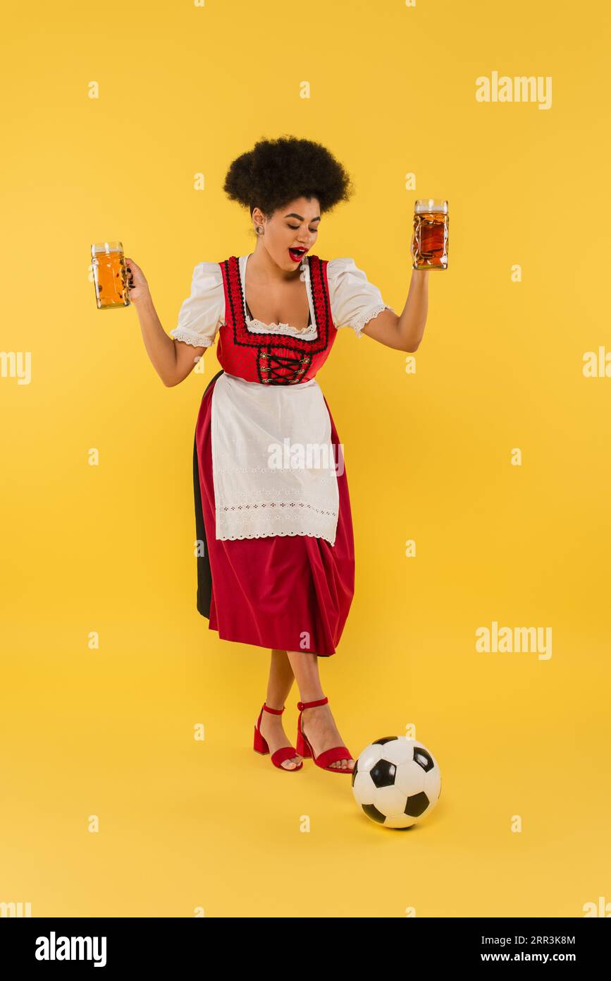joyous african american bavarian waitress in dirndl holding beer mugs ...