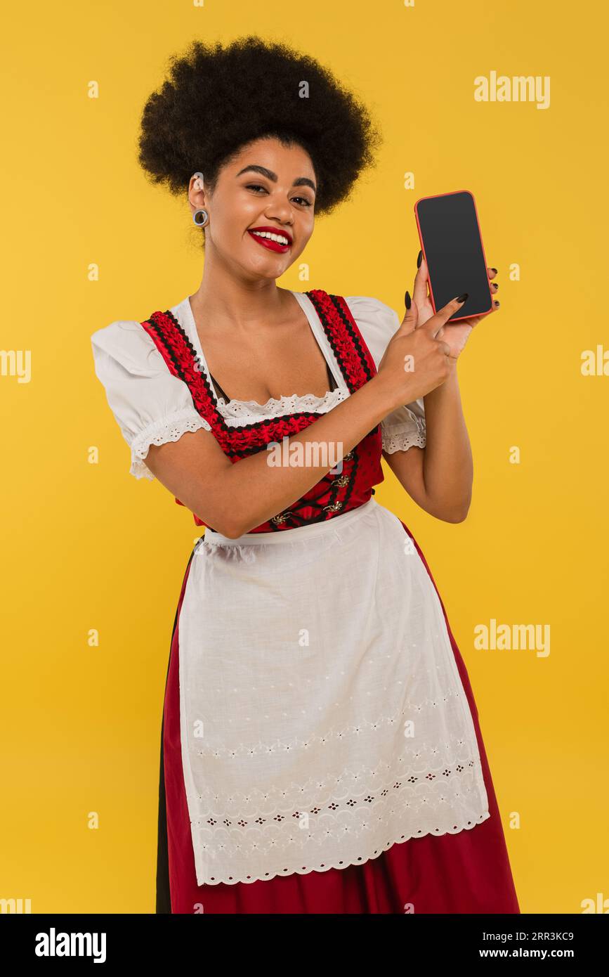 happy african american bavarian waitress in dirndl pointing at blank ...