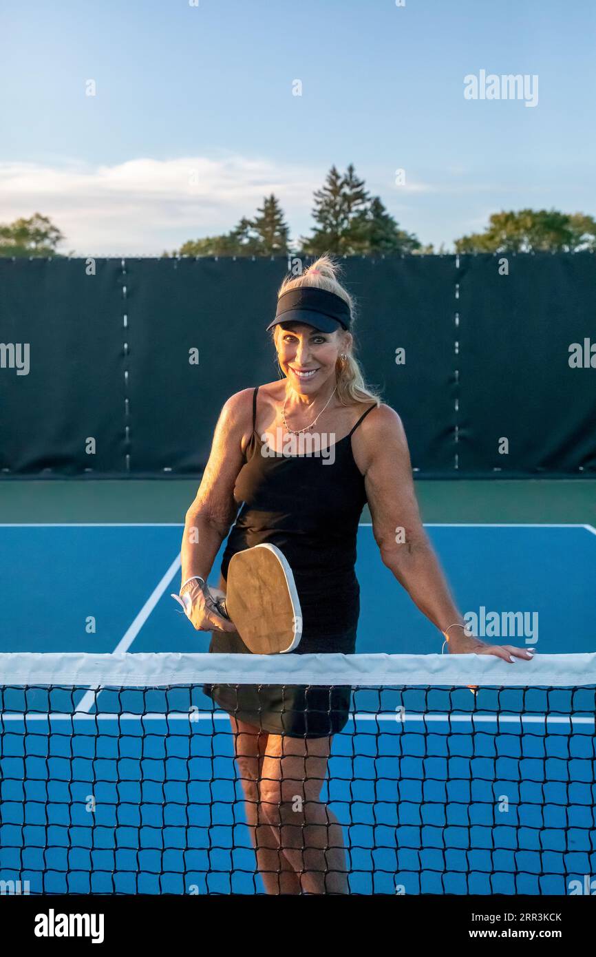 A female pickleball player smiles at the net after a match on a ...