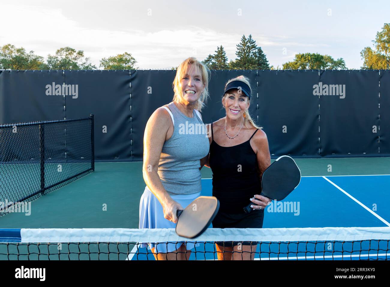 Two female pickleball players pose at the net after a match on a ...