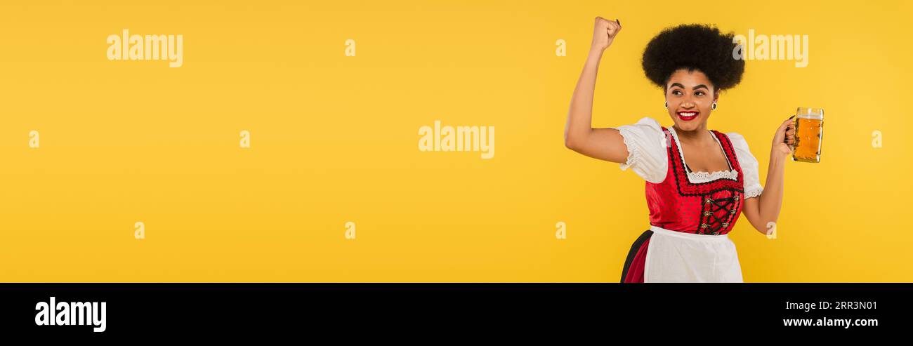 excited african american bavarian waitress with beer mug showing ...