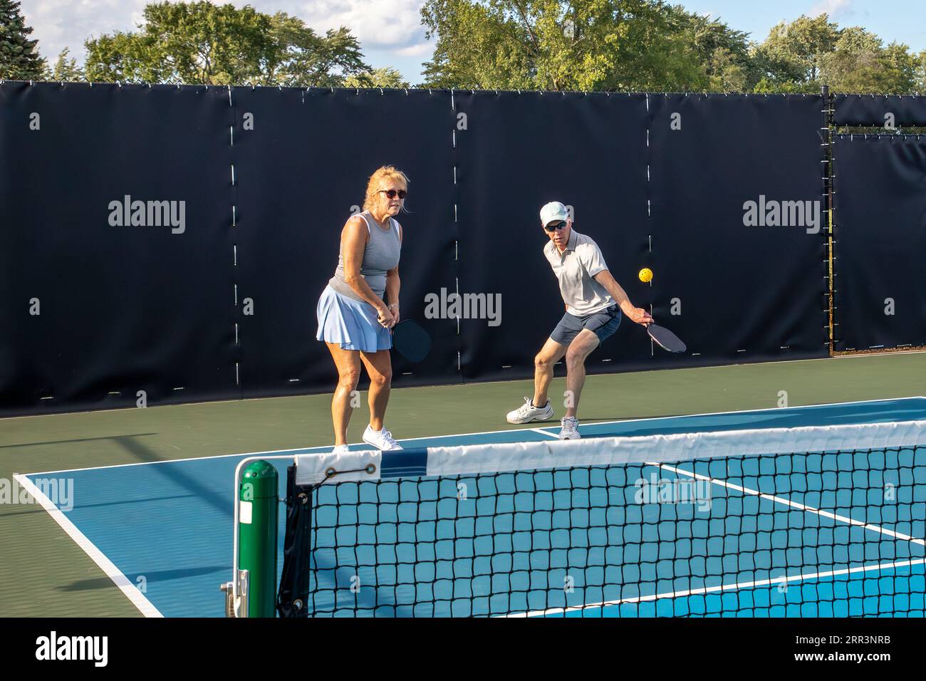 A male pickleball player returns a ball as his female partner stands ...