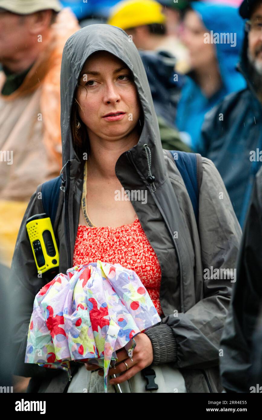 A fed up looking woman with an umbrella in the rainstorm rain and mud ...