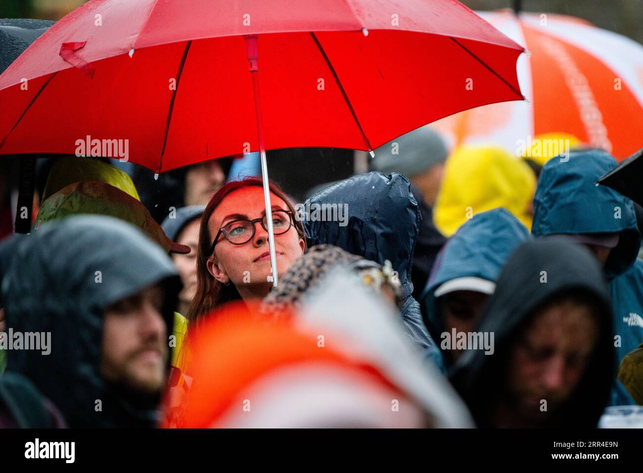 A woman taking shelter under a bright red umbrella in the rainstorm ...