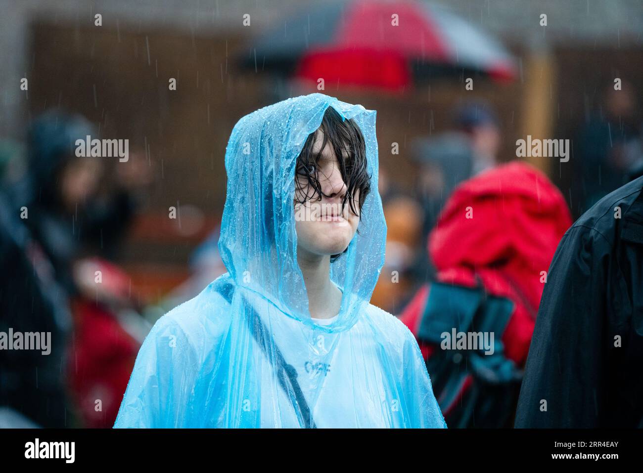 Teenage boy in a disposable rain poncho in the rainstorm rain and mud ...