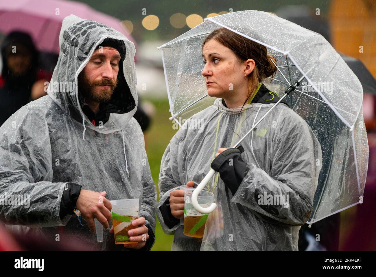 A couple in disposable wets with beers ann umbrella in the rainstorn ...