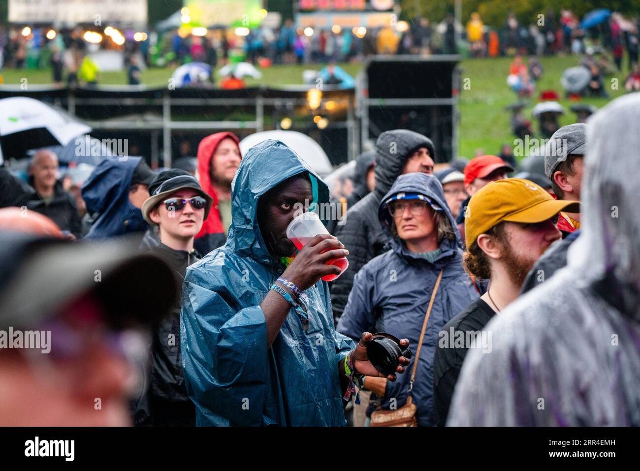 A man with a pint of juice in the crowd in the rain. Green Man Festival ...