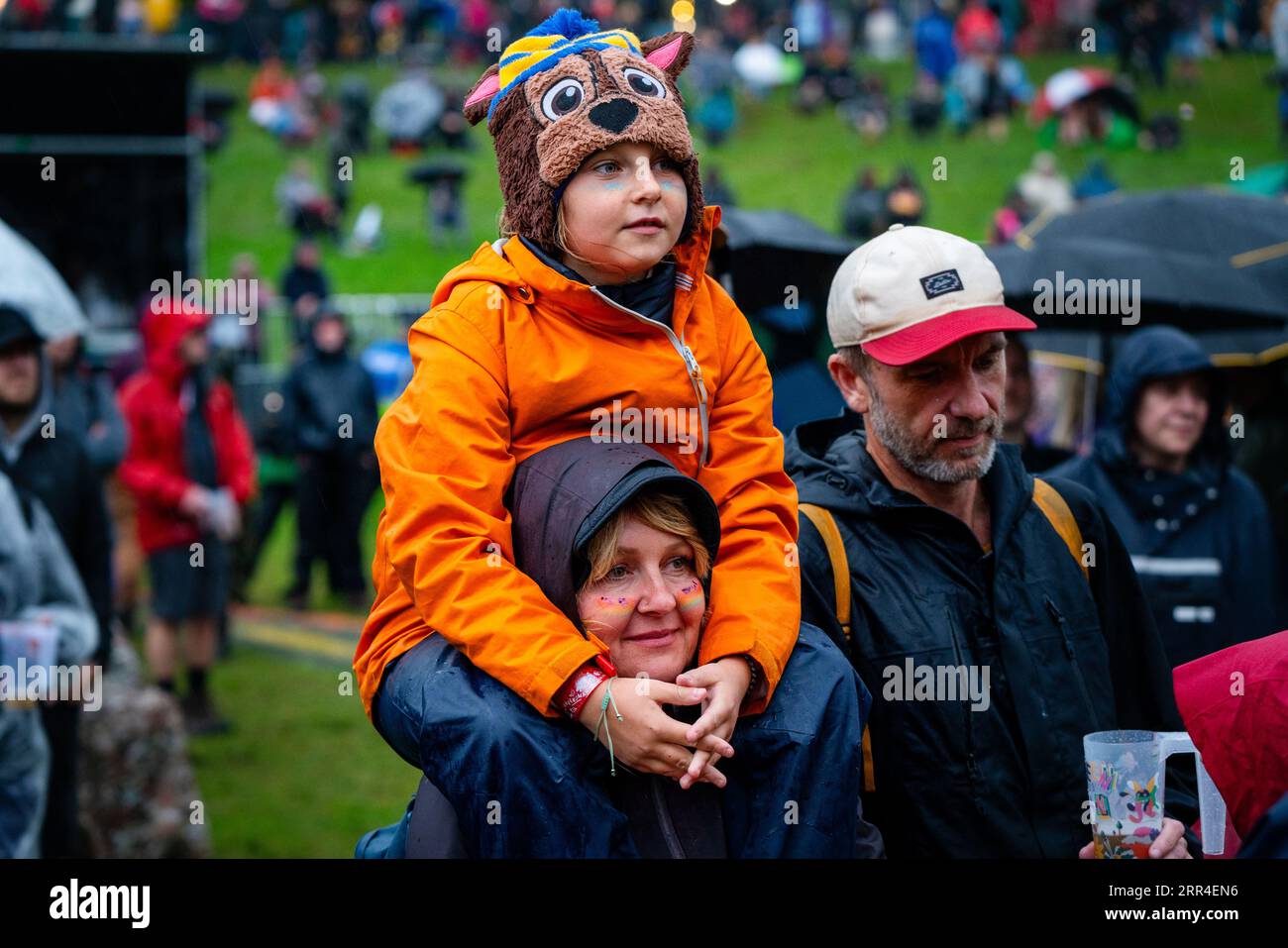 Smiles for a girl on her mum's shoulders in the rainstorm rain and mud ...