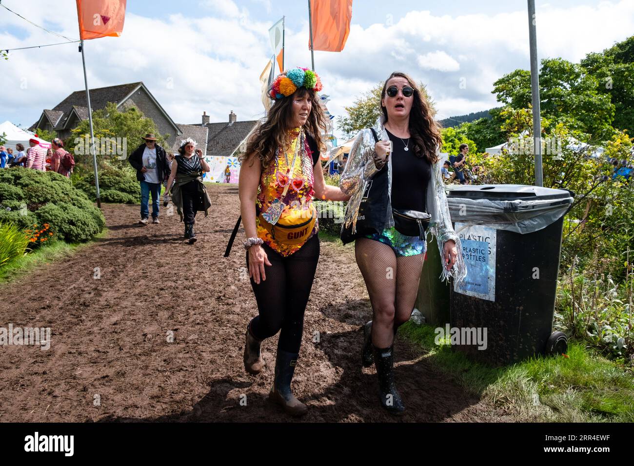 Two bightly dressed woman navigate the mud at Green Man Festival ...