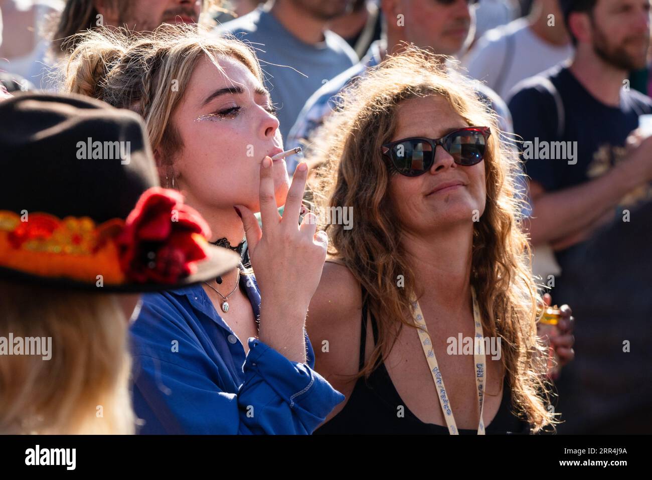 A young woman smokes a roll up cigarette in the crowd at Green Man ...
