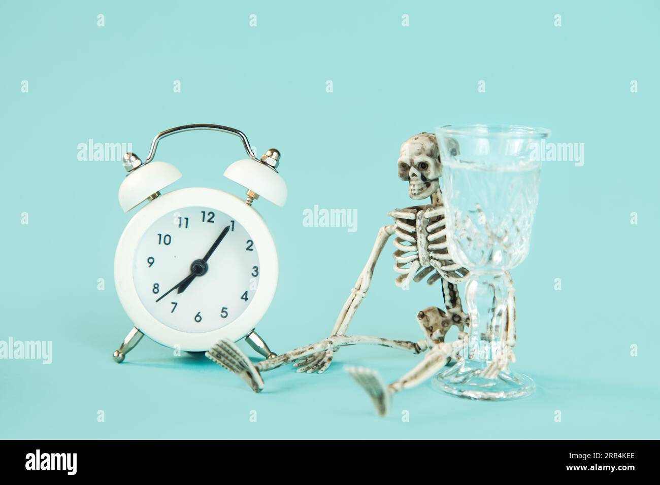 The human skeleton sits with an alarm clock and a glass of vodka. Blue ...