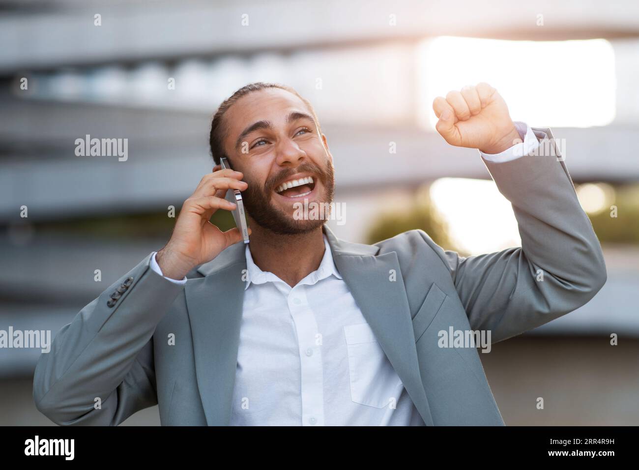 Happy excited young businessman talking on cellphone outdoors and ...