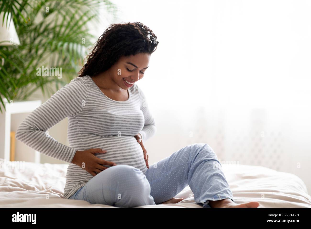 Beautiful black pregnant woman hugging tummy while relaxing on bed at ...