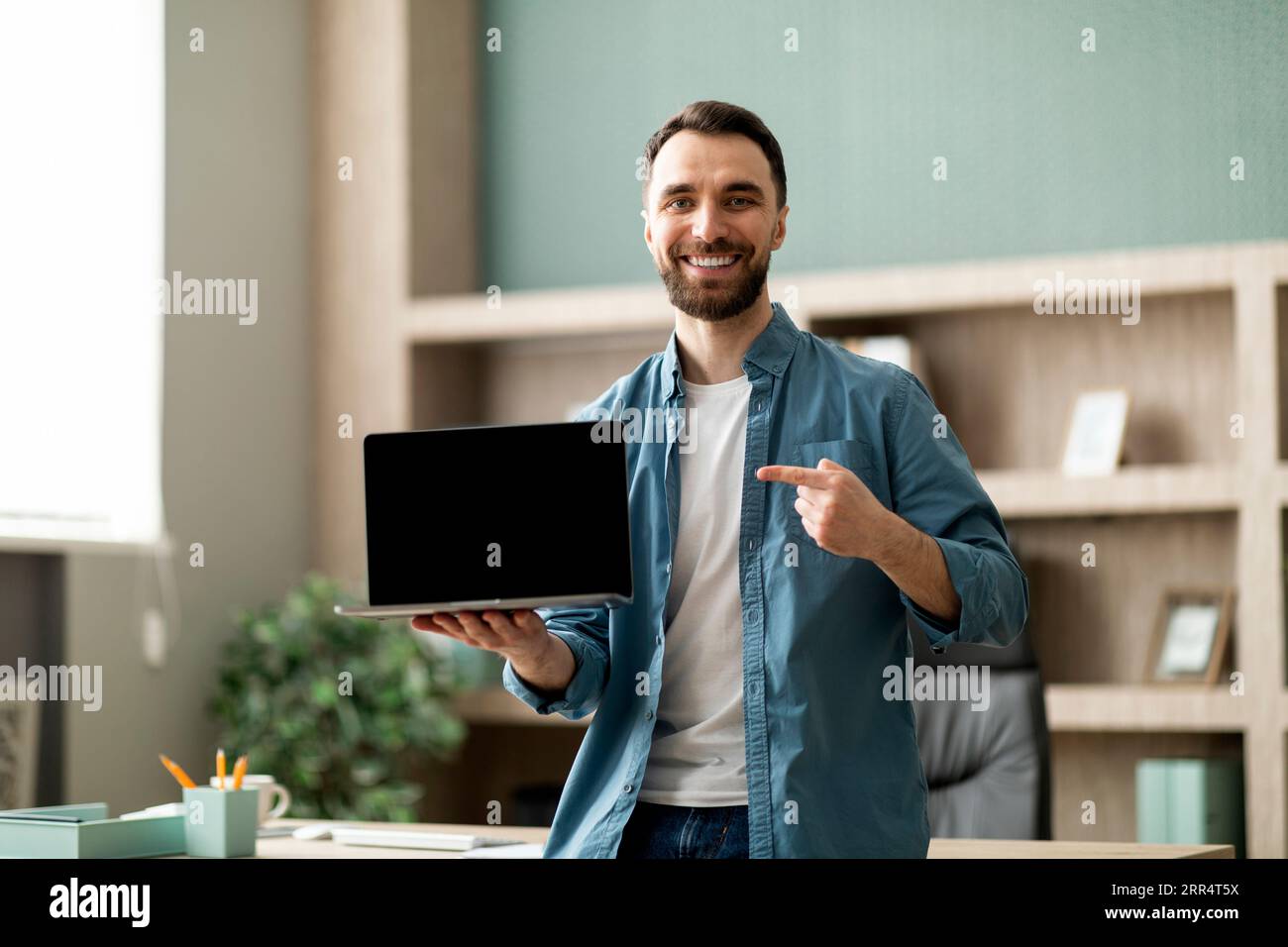 Businessman Pointing Finger At Blank Laptop While Standing Near Desk In ...
