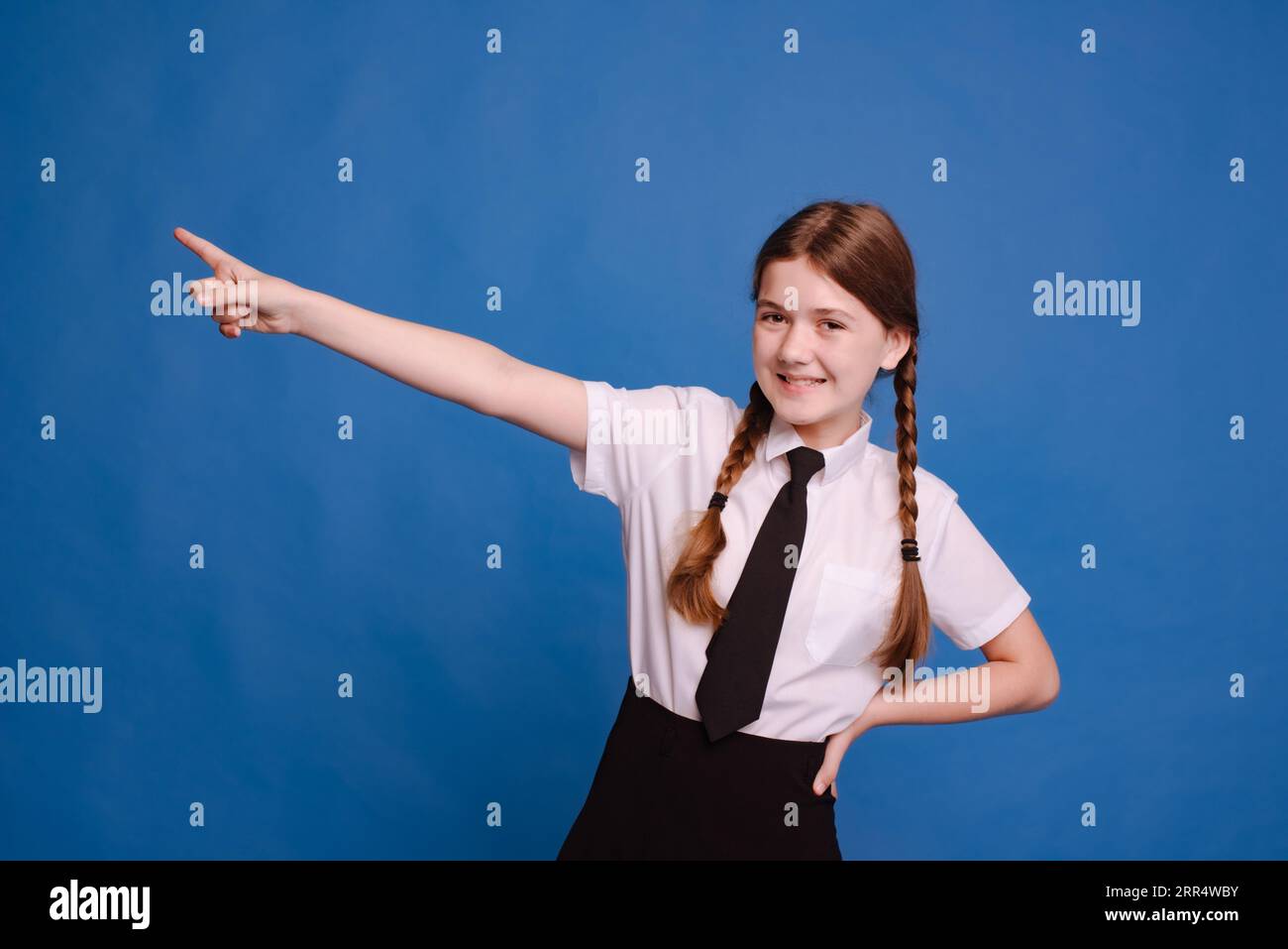 school girl point finger with hairstyle two braids in uniform over blue ...