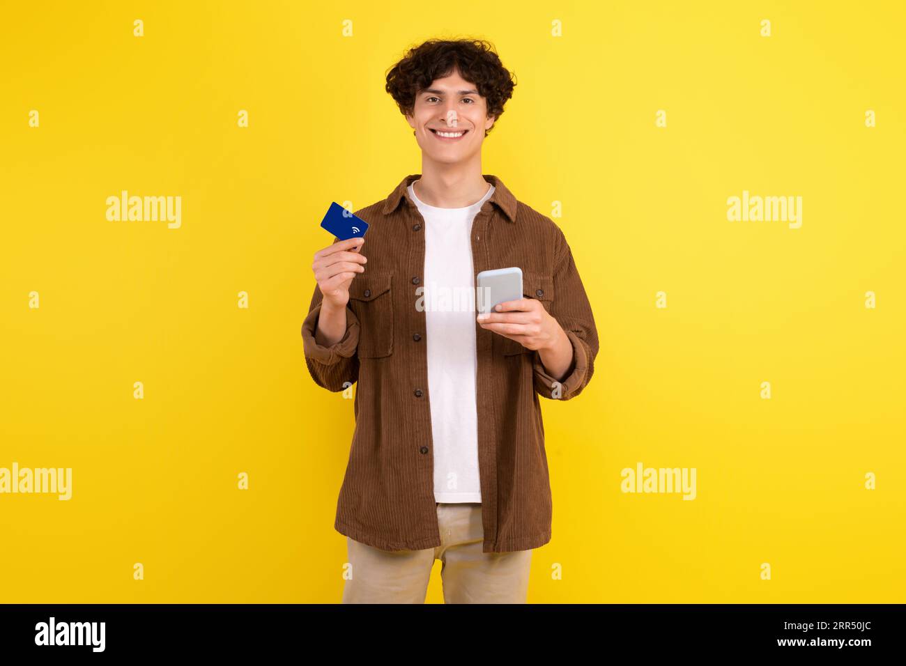 Happy guy holding credit card and smartphone over yellow background ...