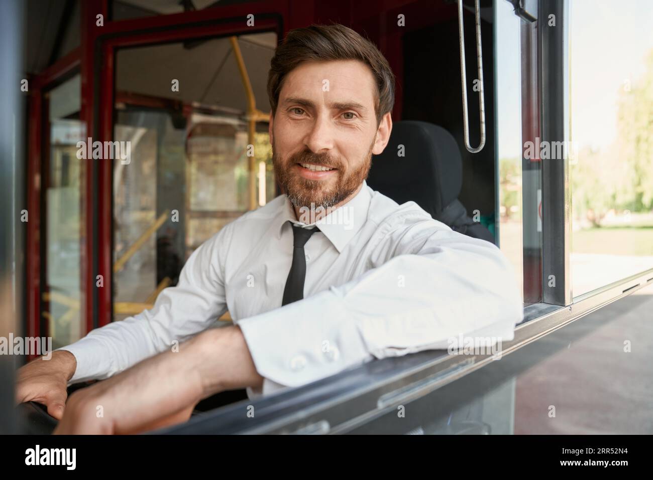 Confident bearded man sitting in driver's seat with one arm resting on ...