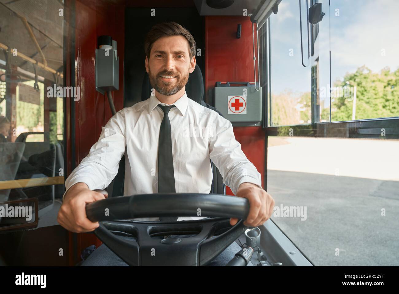 Cheerful elegant driver looking to camera, while driving bus at sunny ...