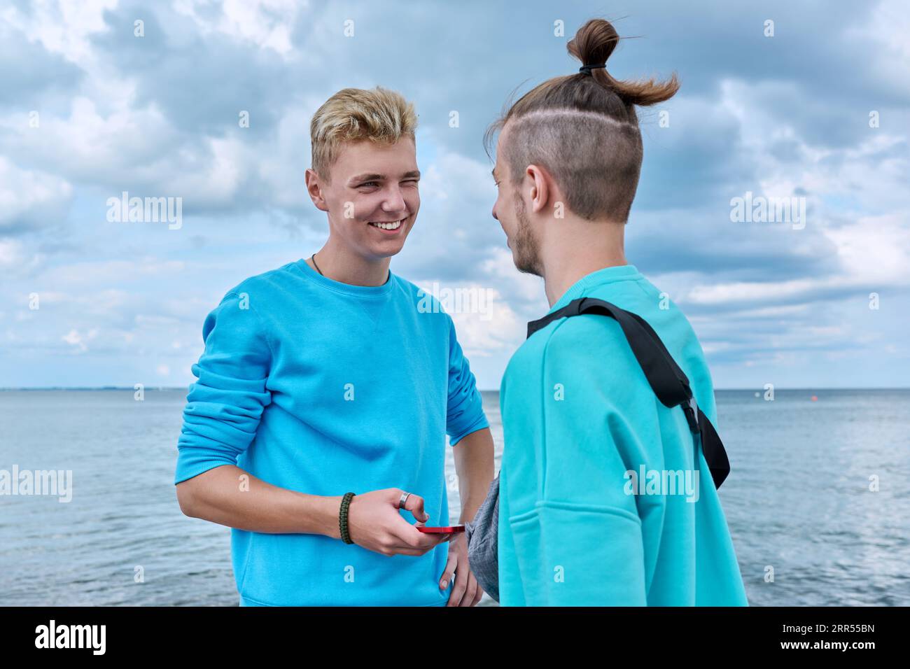 Two friends cheerful laughing young guys with smartphone, beach outdoor ...