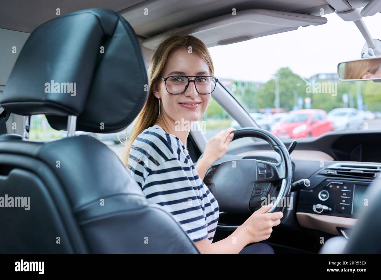 Teenage girl driver in glasses sitting behind wheel of car, looking at ...