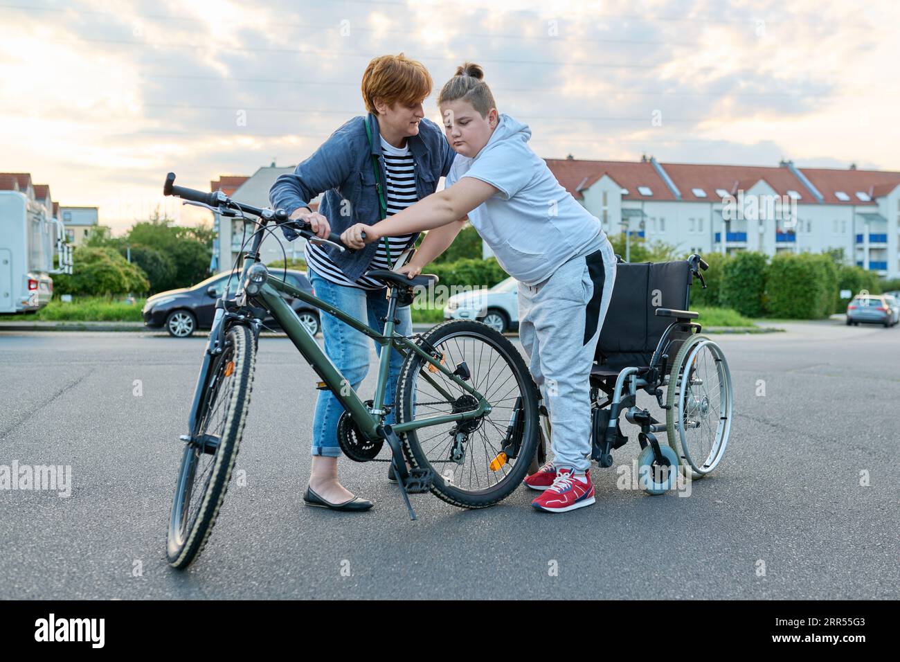 Boy transfers from wheelchair to bicycle, mother helping child to ...