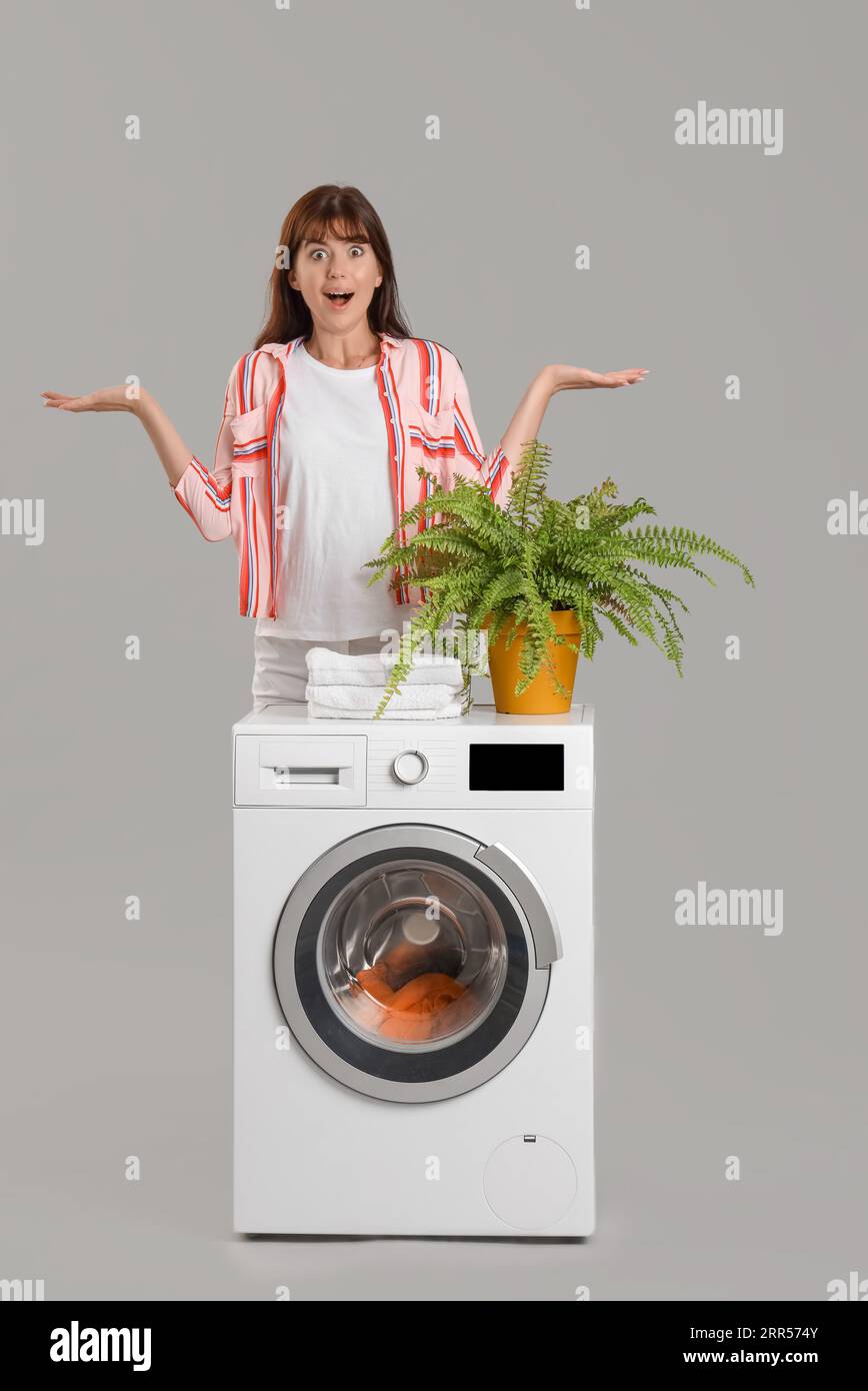 Surprised young woman with washing machine on grey background Stock ...