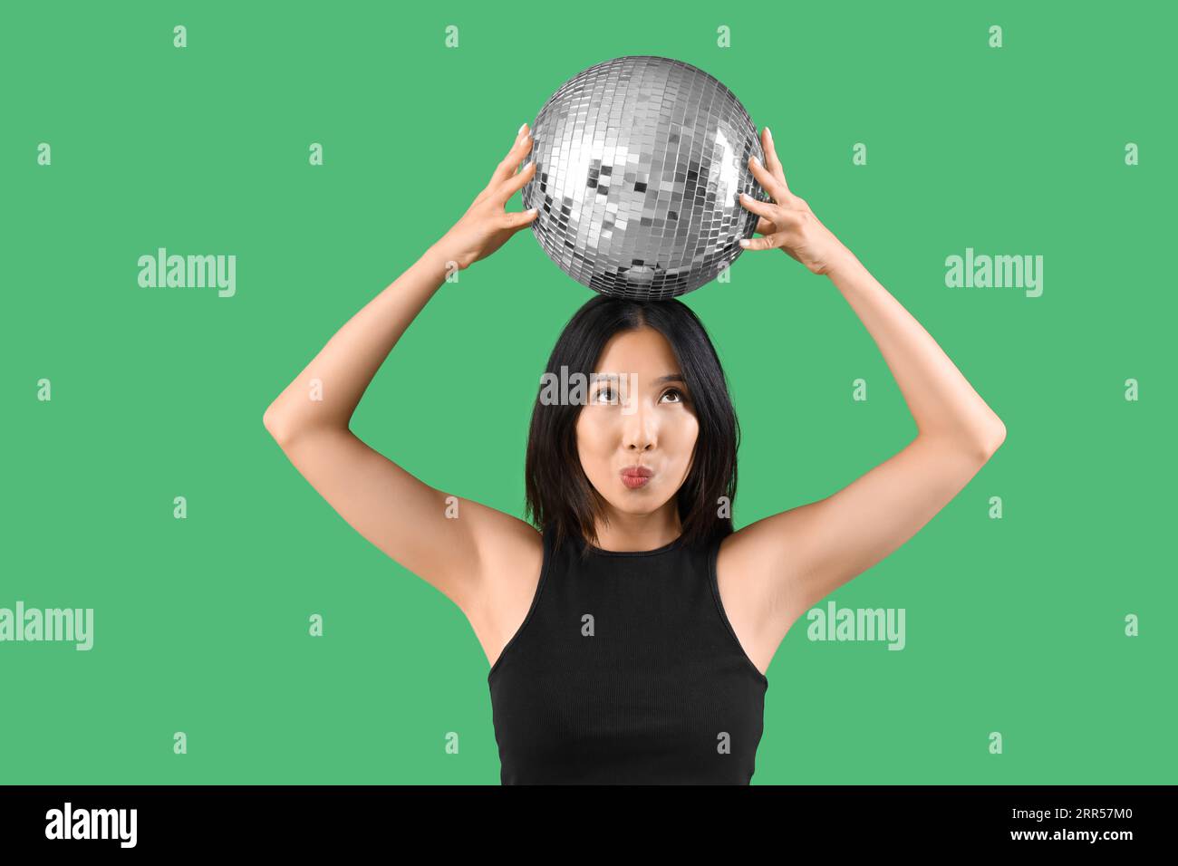 Thoughtful beautiful Asian woman with disco ball on green background ...