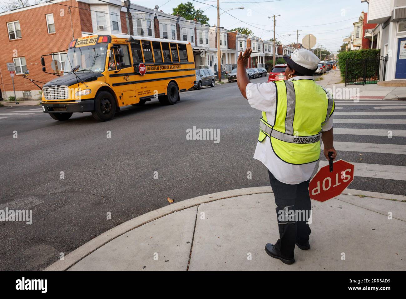 Crossing guard Pamela Lane waves a school bus passing her intersection ...
