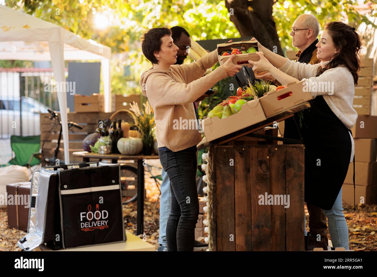 Fruit and vegetable seller giving organic produce box to young delivery ...