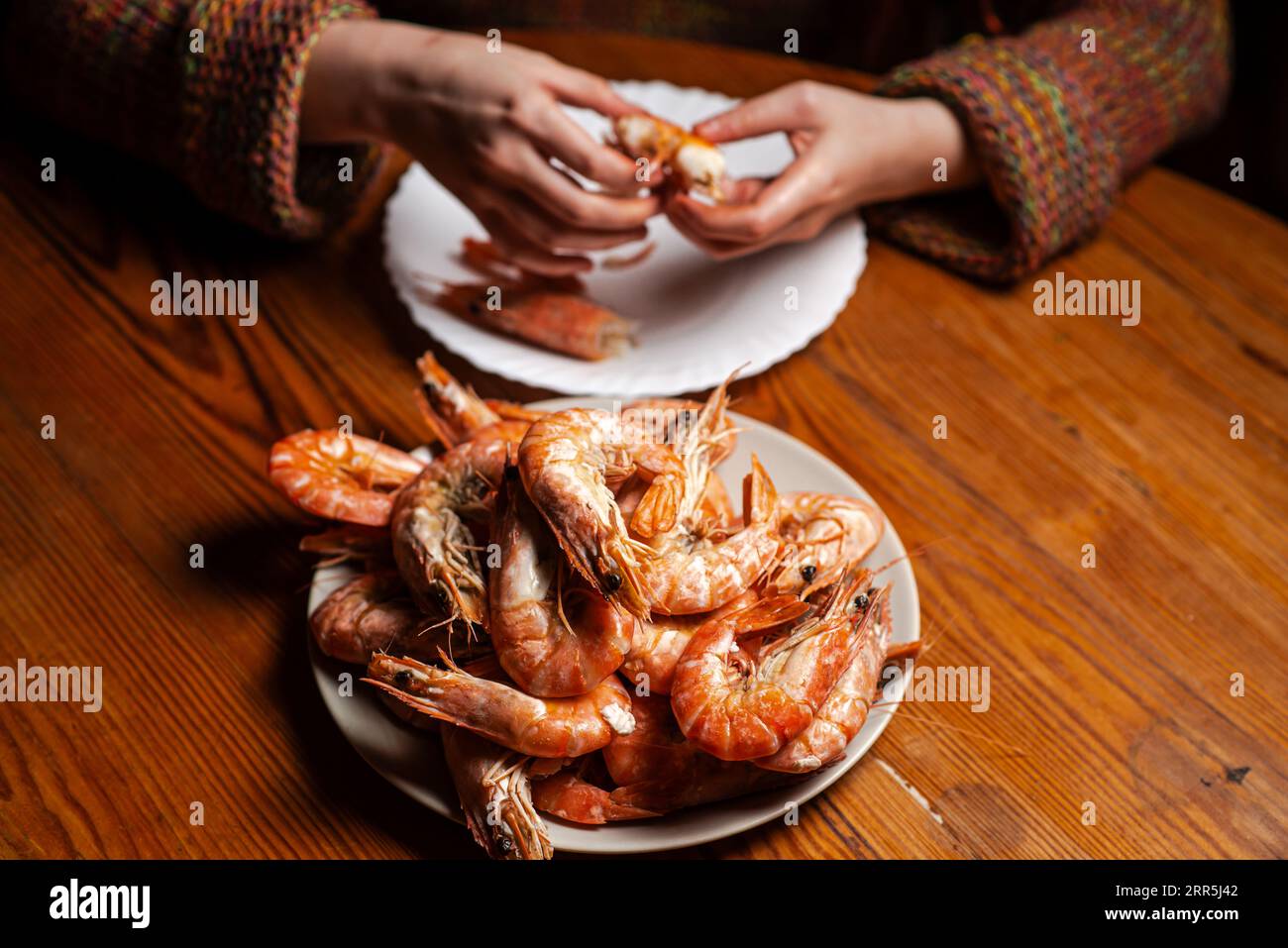 Large cooked king prawns on the table. An unrecognizable man is eating ...