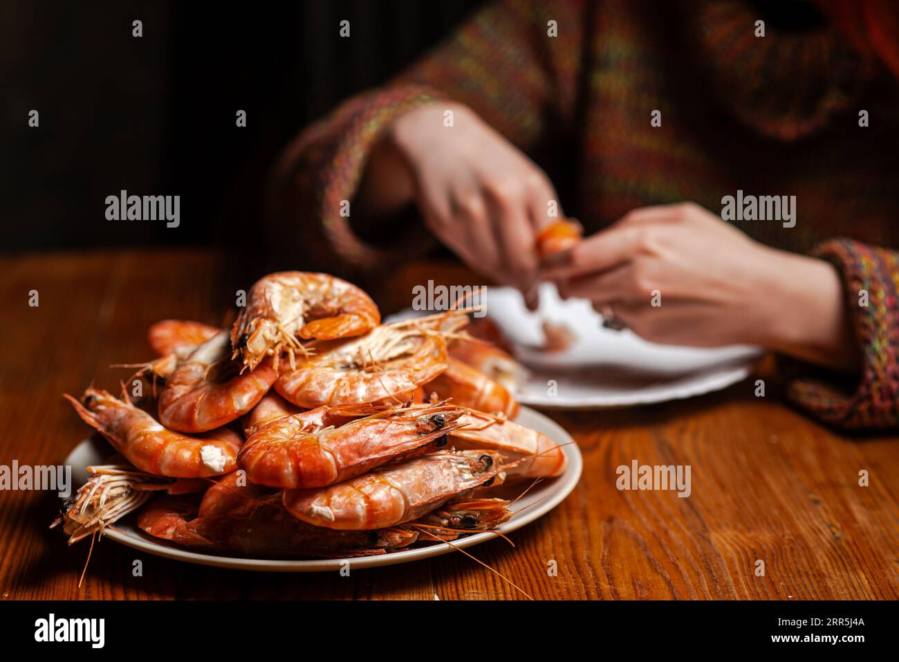 Large cooked king prawns on the table. An unrecognizable man is eating ...