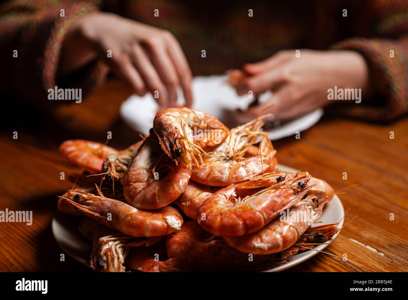 Large cooked king prawns on the table. An unrecognizable man is eating ...