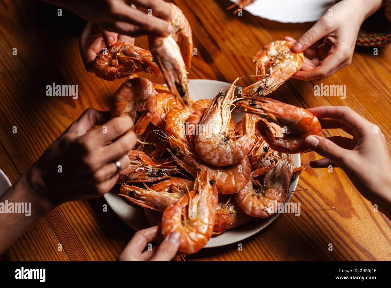 Large boiled king prawns on the table. Recognizable people eat shrimp ...