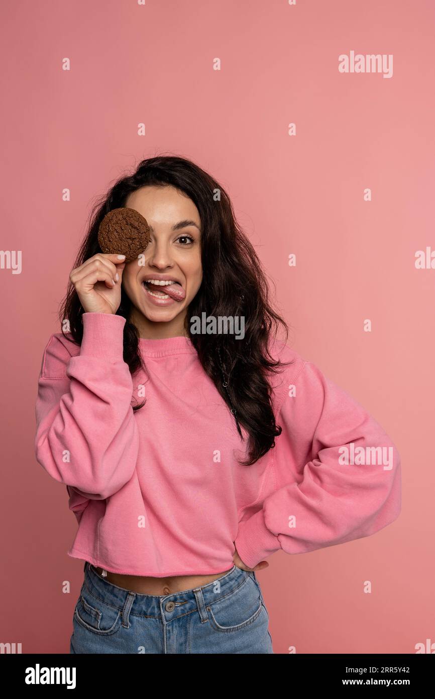 Playful cute brunette covering one eye with an oatmeal cookie while ...