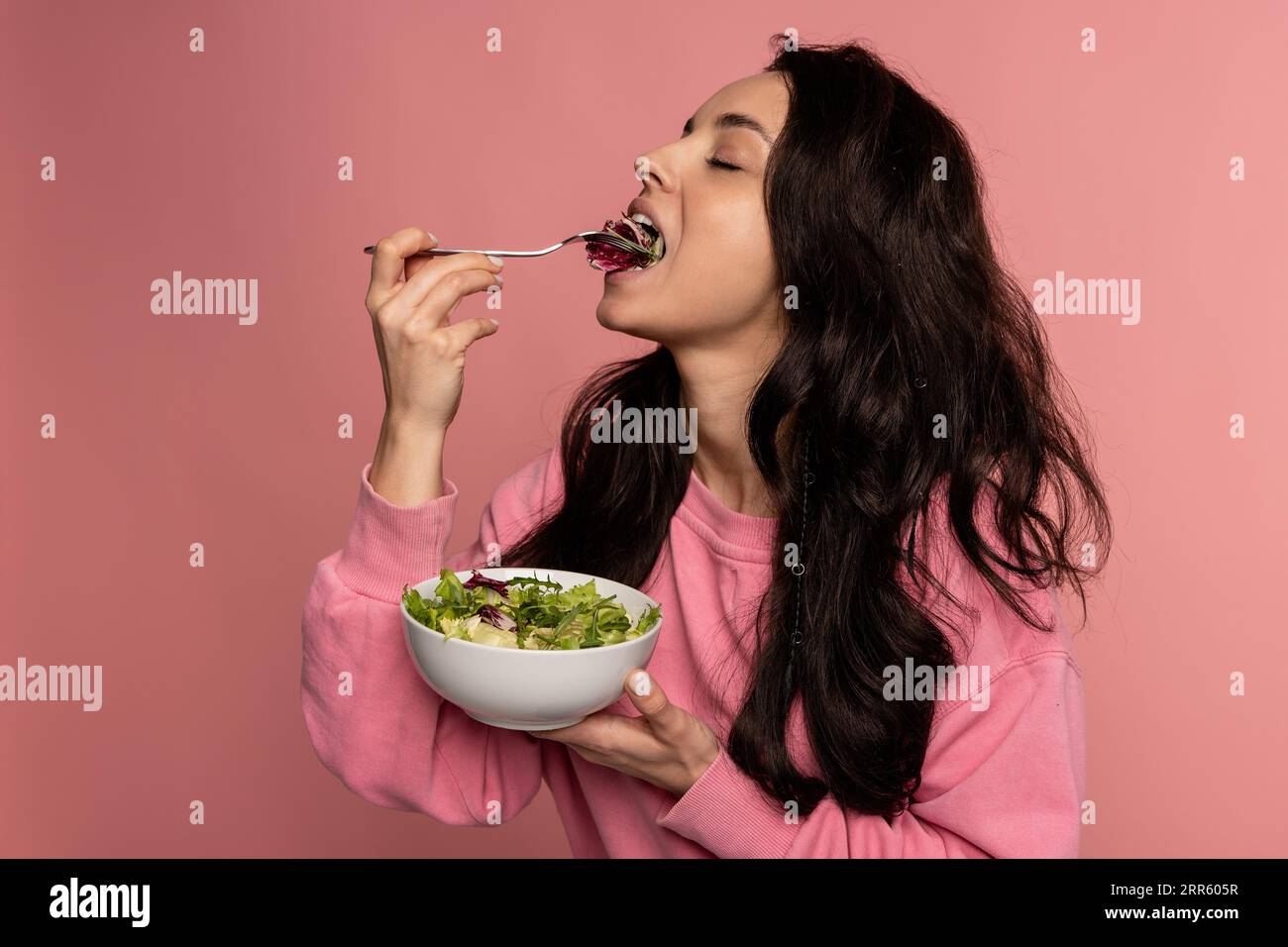 Young woman snacking on a portion of a vegetable dish with her eyes ...