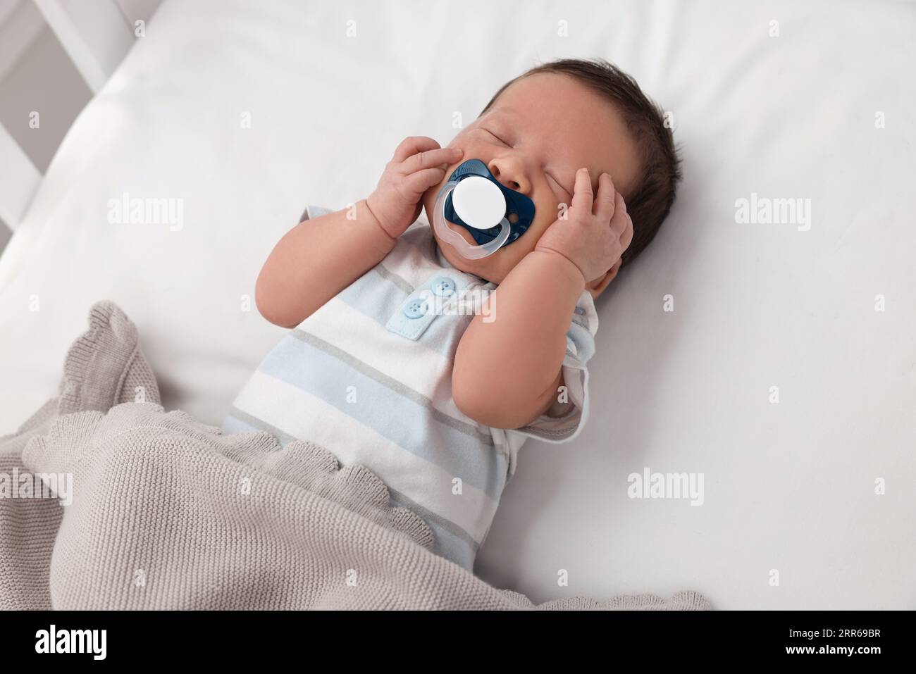 Cute newborn baby with pacifier sleeping under blanket in crib. Bedtime ...
