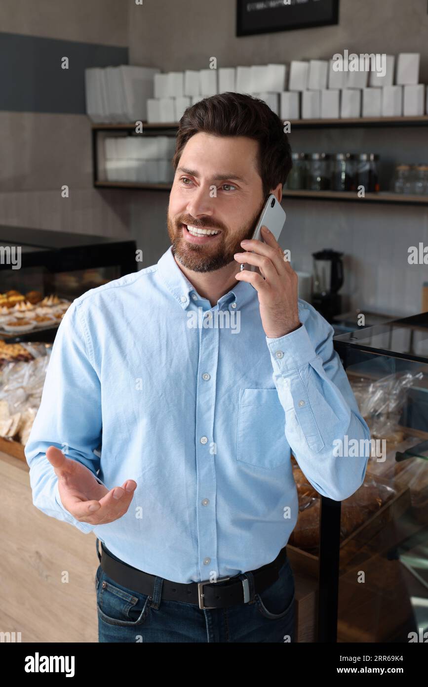 Happy business owner talking on phone in bakery shop Stock Photo - Alamy