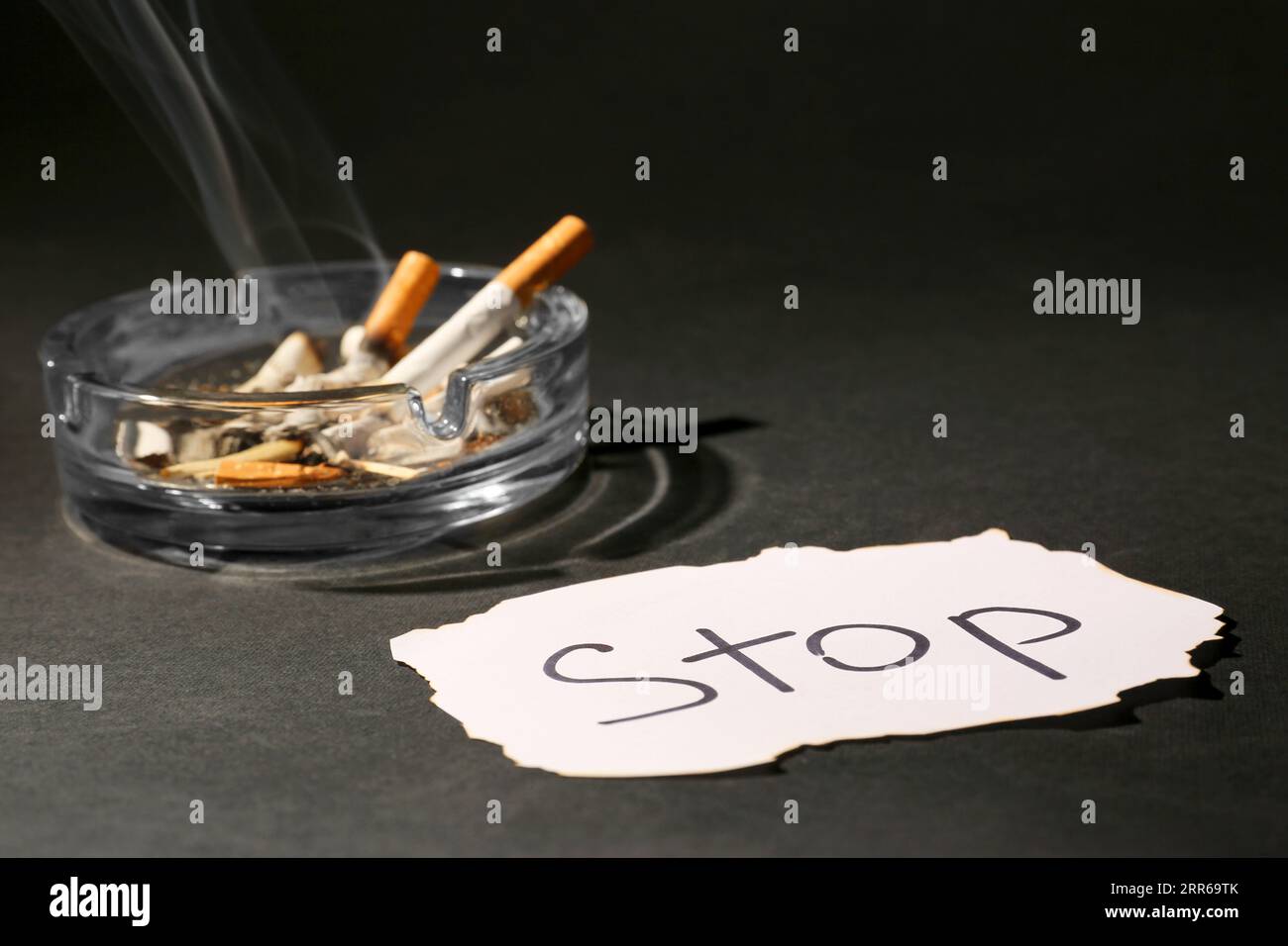 Ashtray with burnt cigarettes and word Stop written on paper on black ...