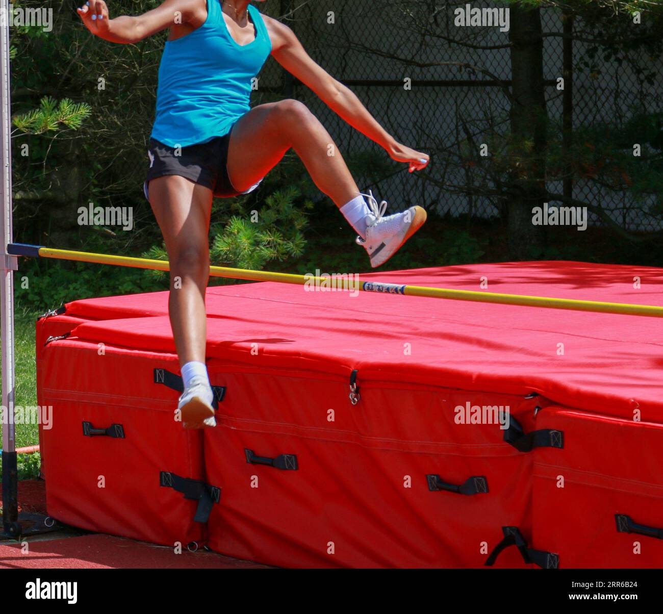 One teenage girl jumping over a yellow high jump bar on to red mats ...