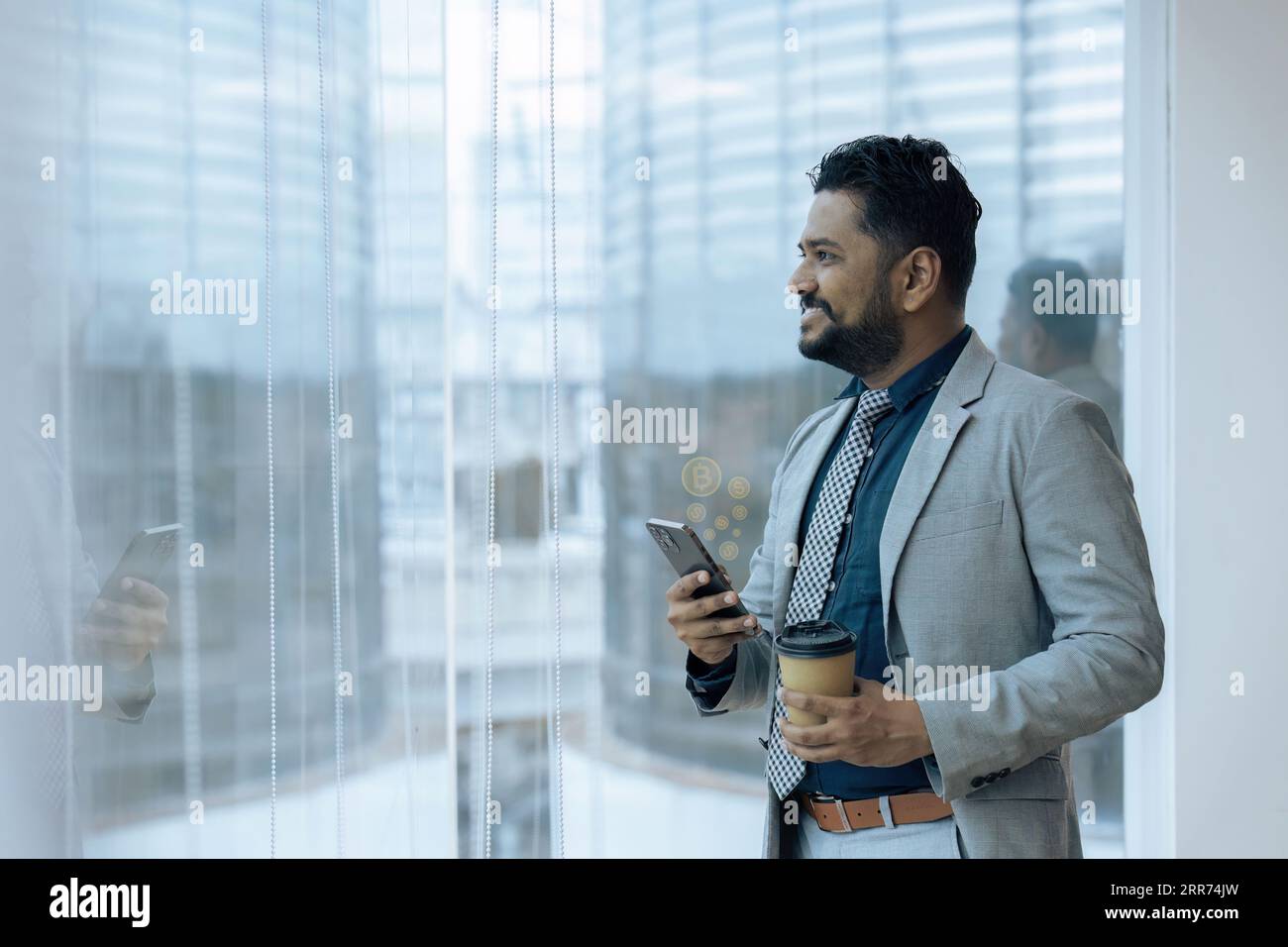 Indian businessman standing next to window using mobile phone wile ...
